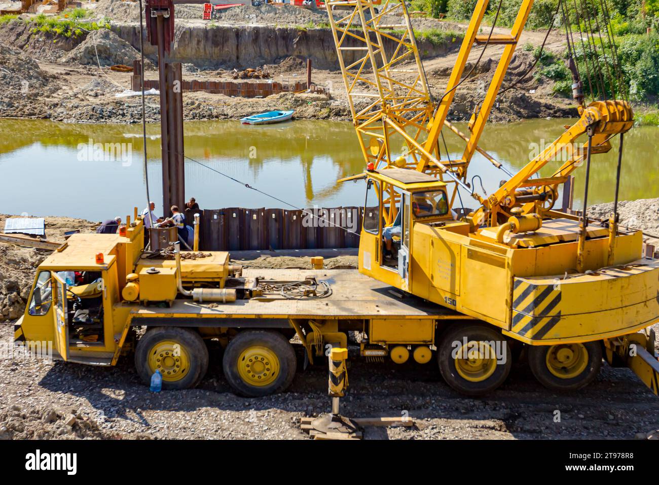 Yellow obsolete mobile crane with pneumatic hammer installing metal ...