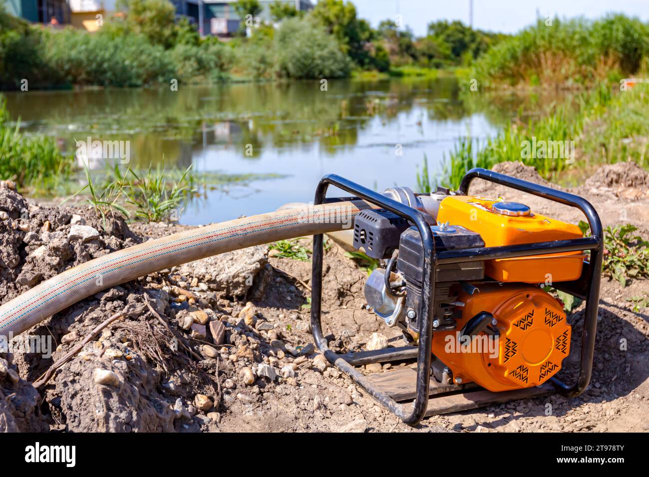 Orange motor pump with long hose for filling tank with water placed on coast, bridge ...