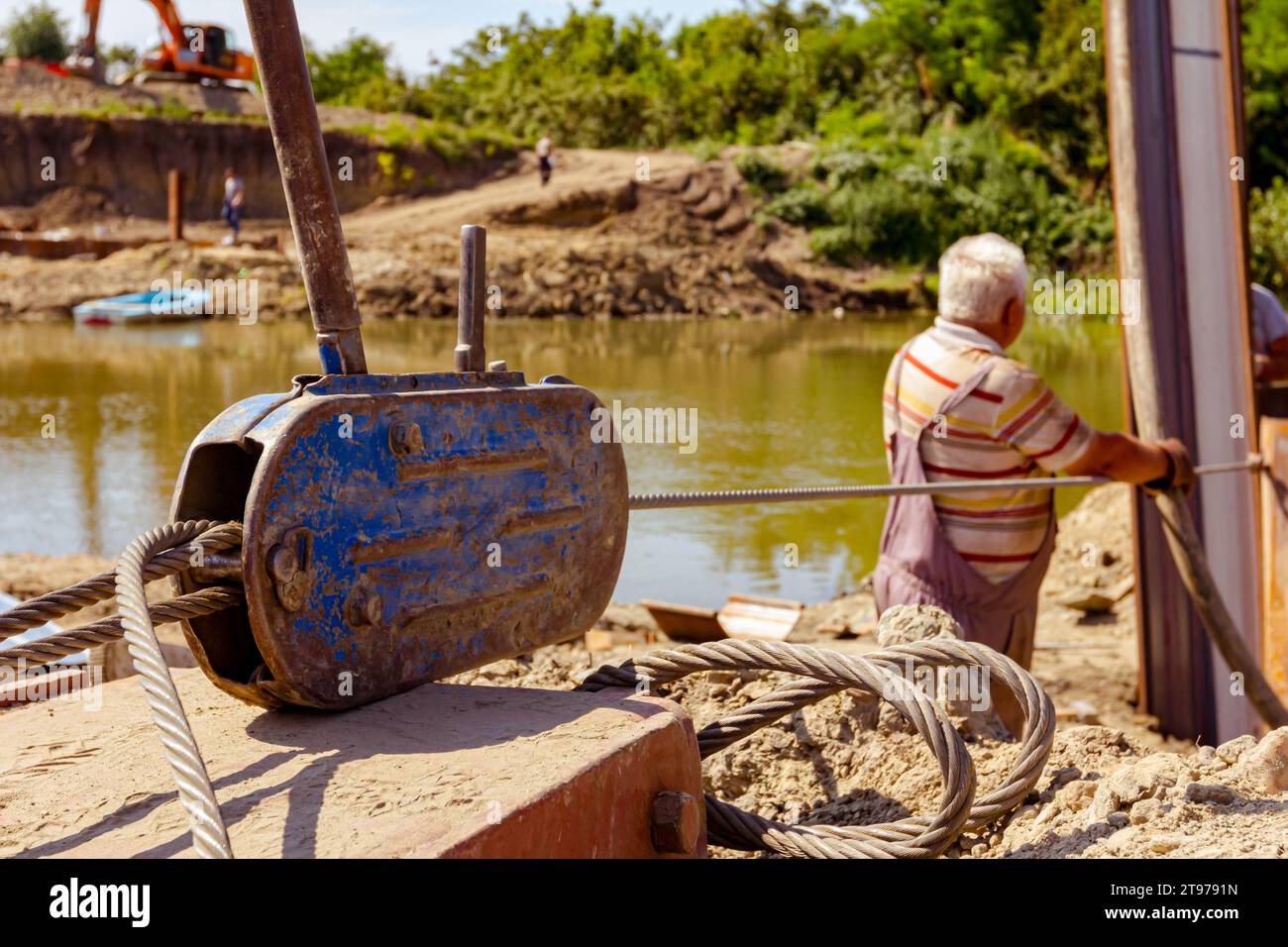 Worker uses hand cable puller winch with two hooks and metal crank ...