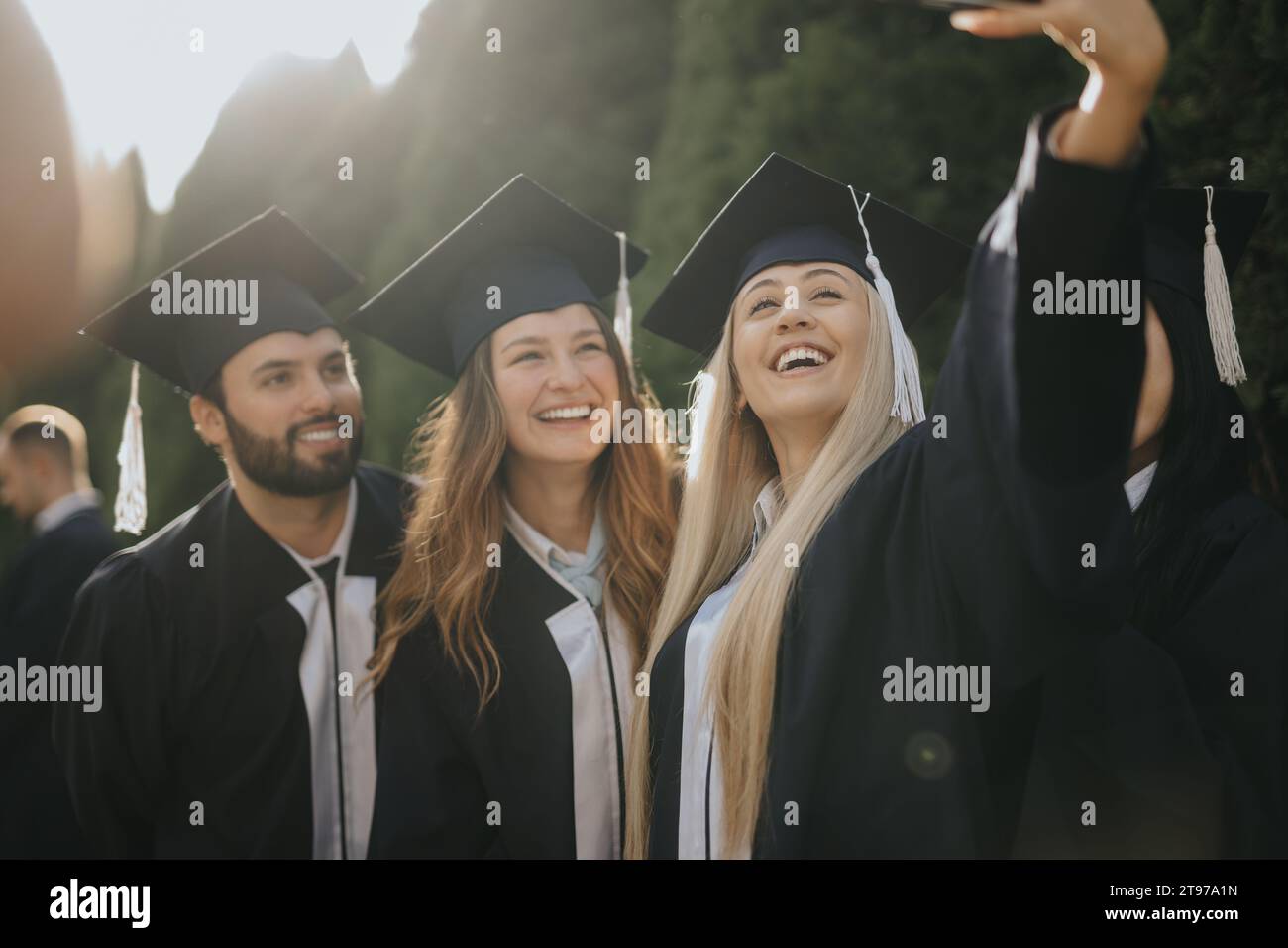 Multiethnic university students celebrate graduation in a sunny park ...