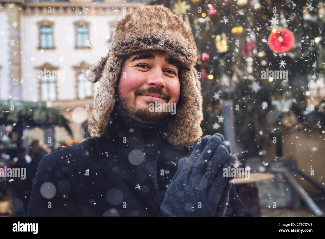Man in fur hat and winter coat smiling gently, snowflakes falling ...