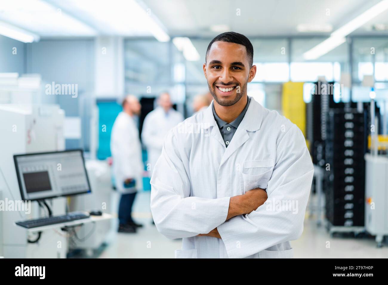 Confident technician smiling with arms crossed while colleagues are ...