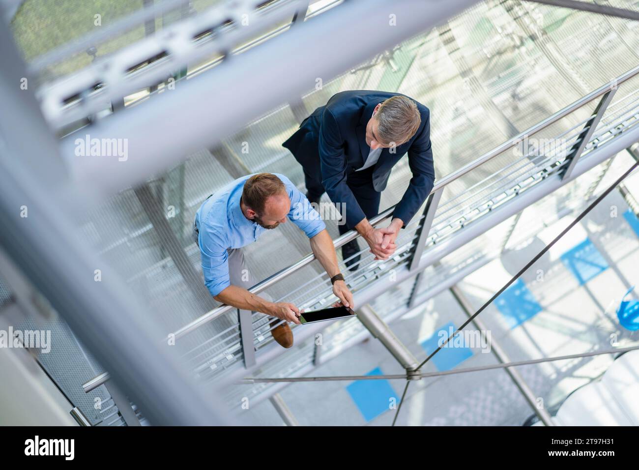 Colleagues leaning on railing in office building discussing business ...
