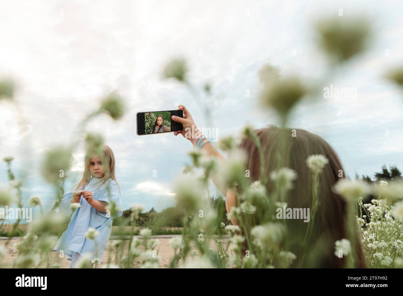 Woman clicking selfie through smart phone in front of girl standing at ...