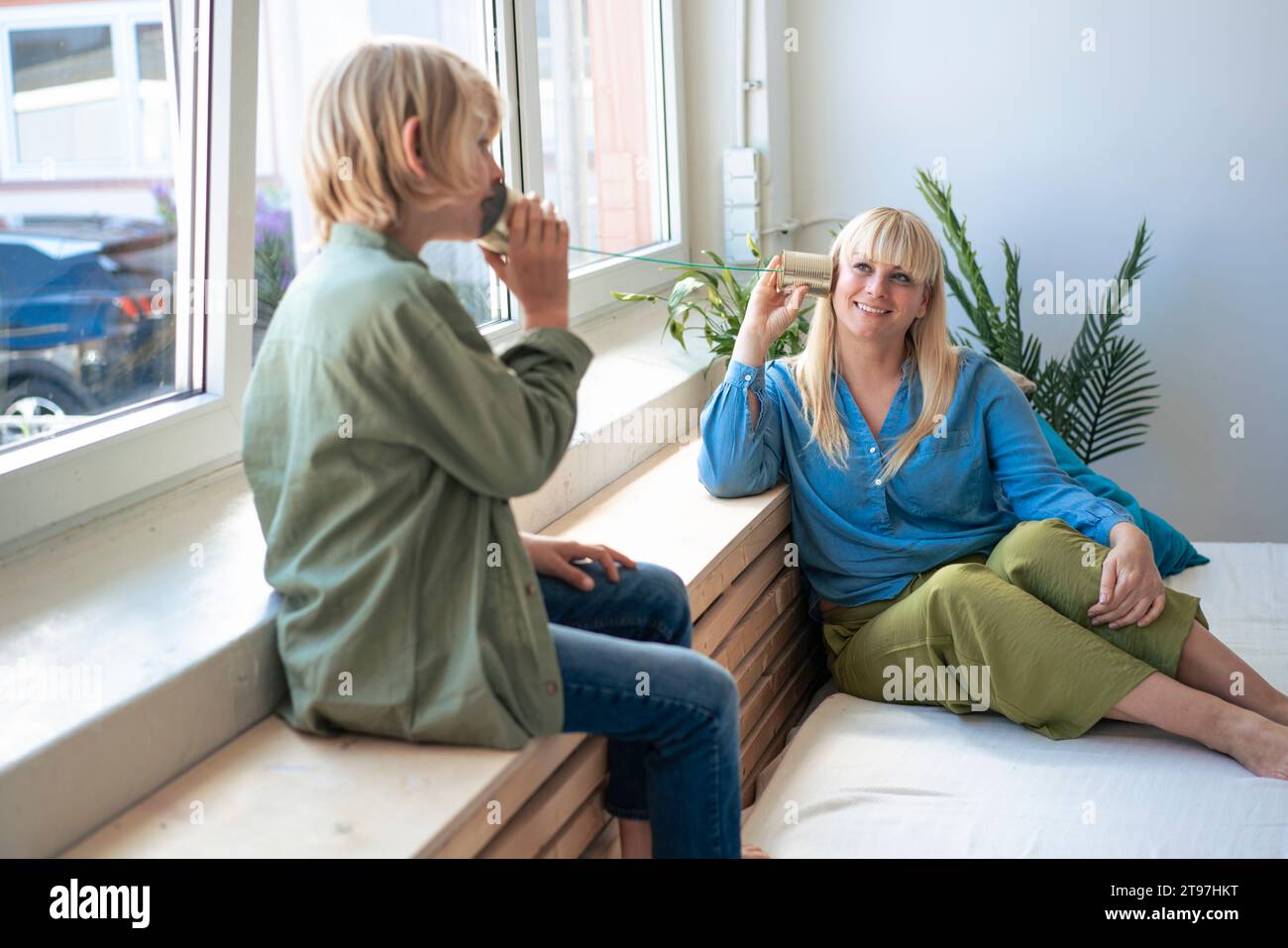 Boy talking through tin can phone with smiling mother at home Stock ...