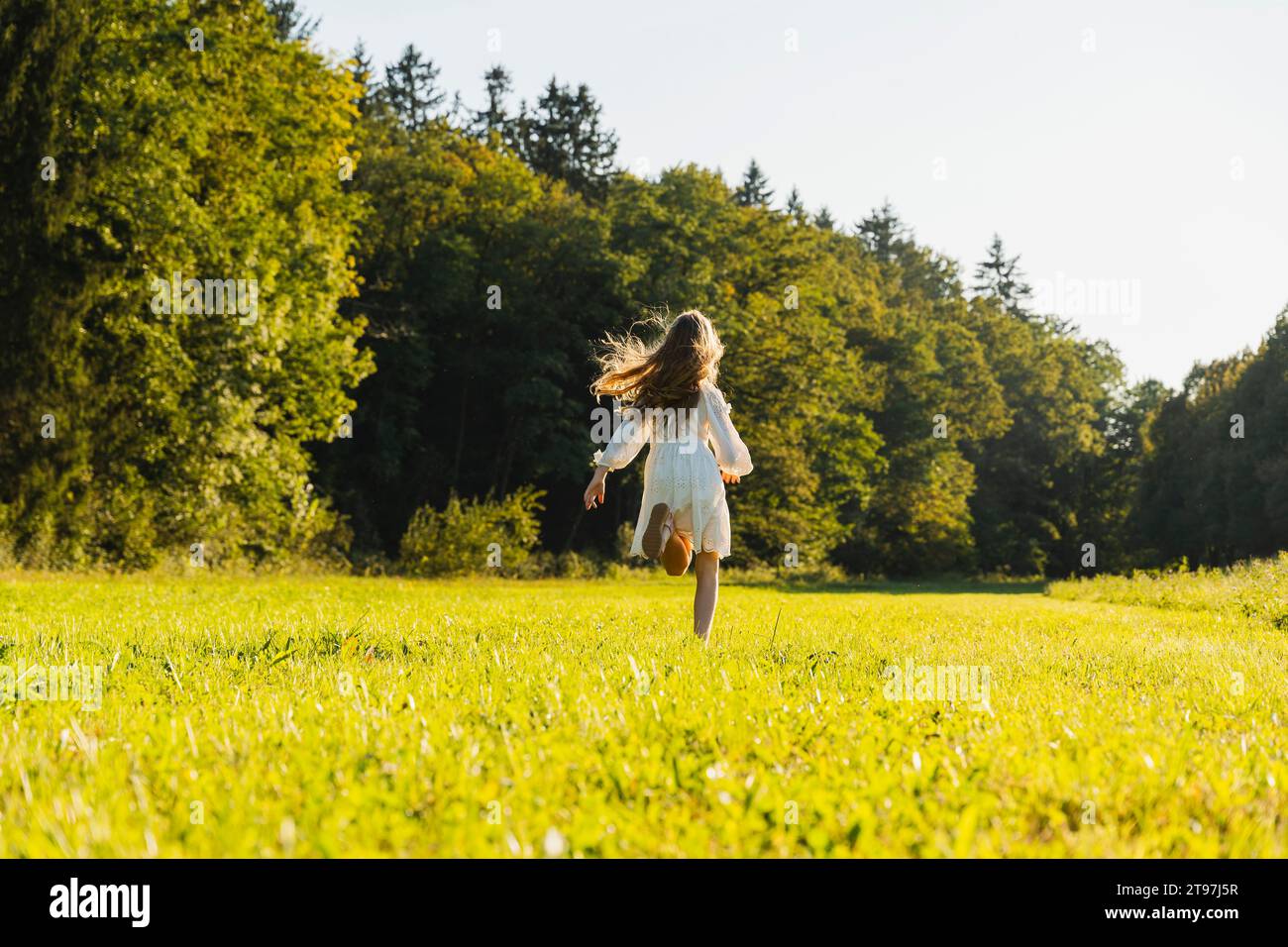Happy girl running in front of trees in meadow Stock Photo - Alamy