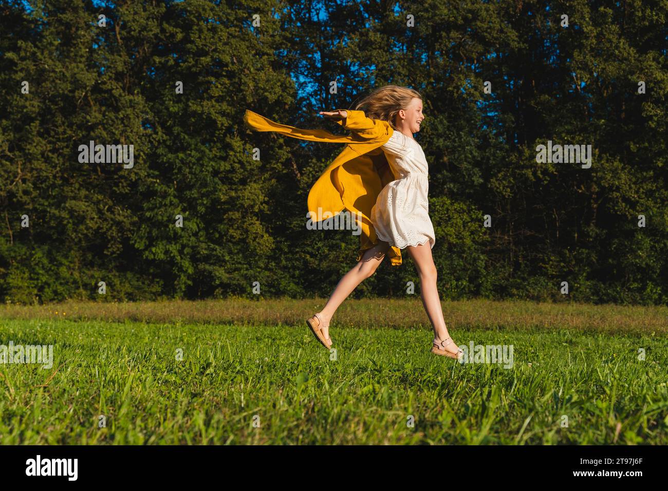 Cheerful girl jumping on grass in front of trees Stock Photo - Alamy