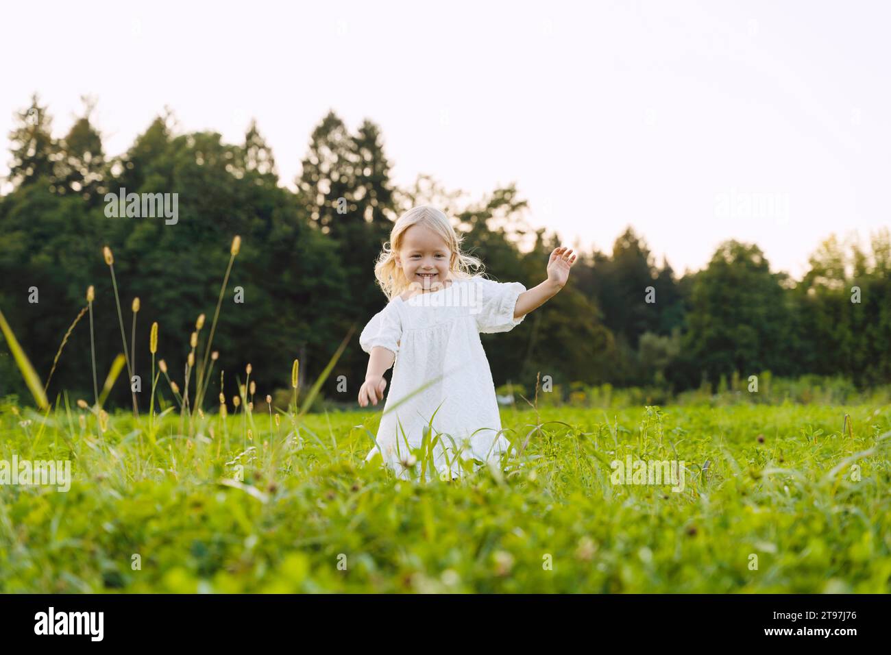 Smiling blond girl running in front of trees Stock Photo - Alamy