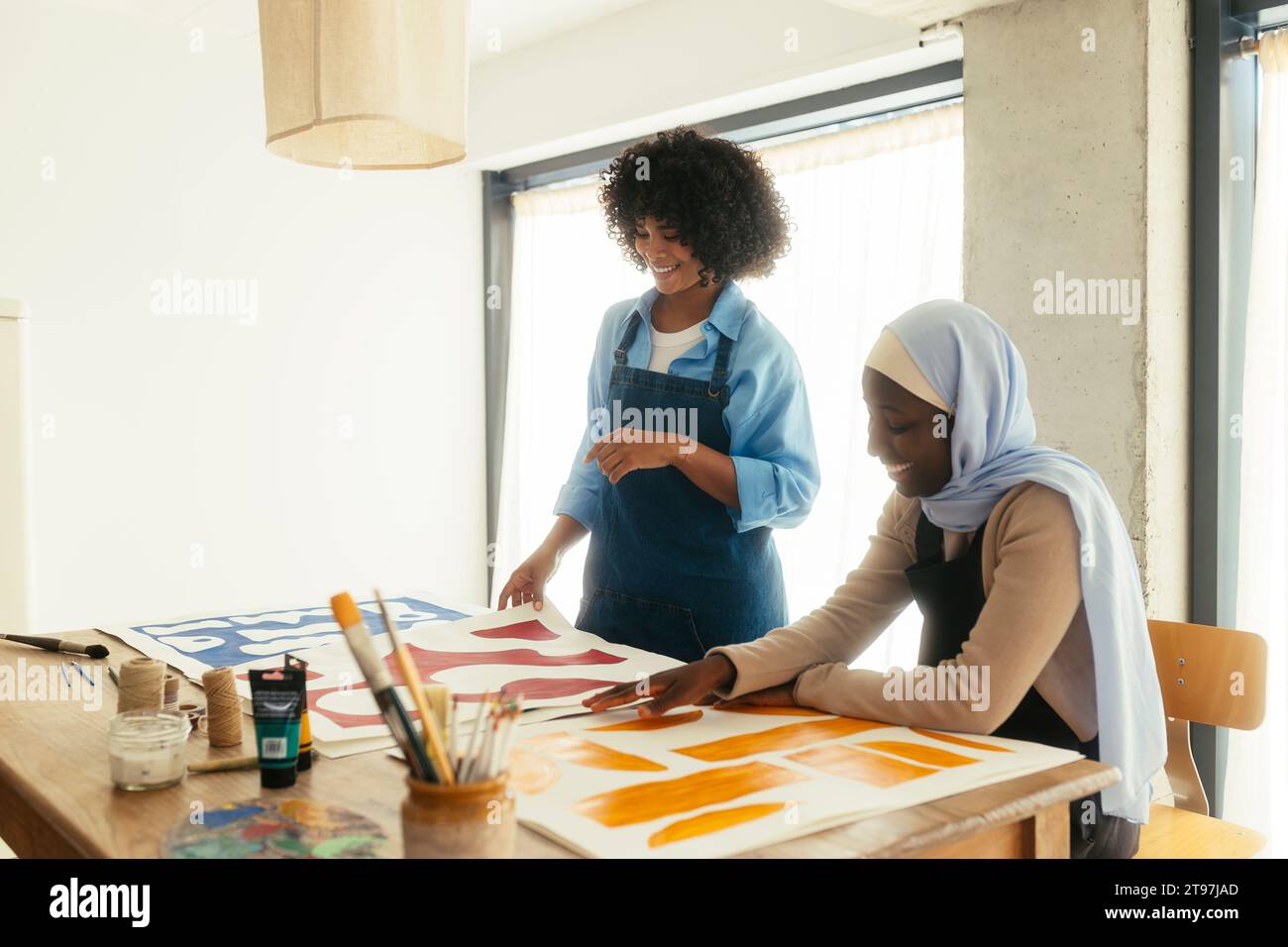 Smiling artists looking at paintings on desk in studio Stock Photo - Alamy