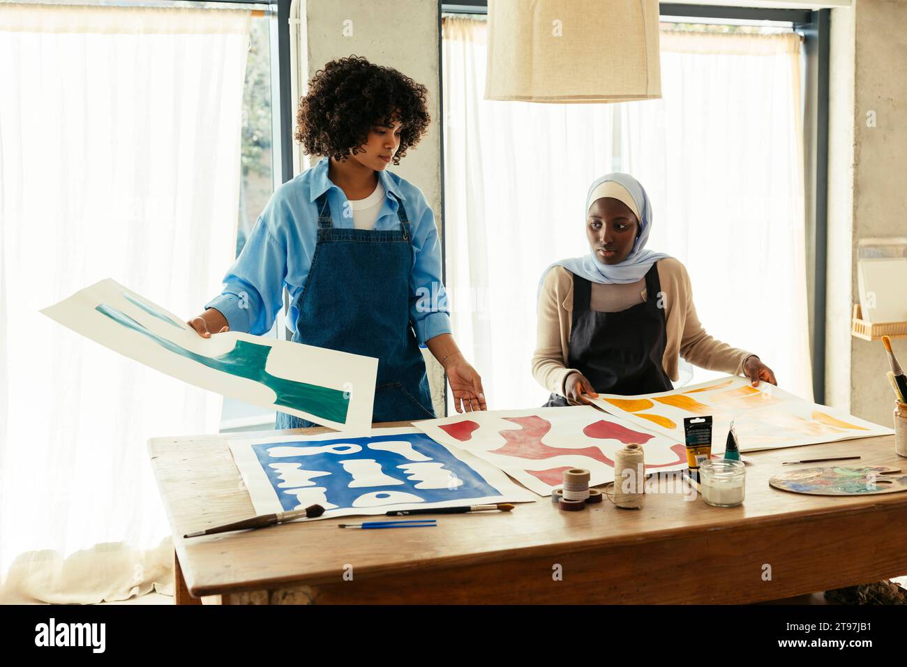 Artists comparing paintings at desk in studio Stock Photo - Alamy