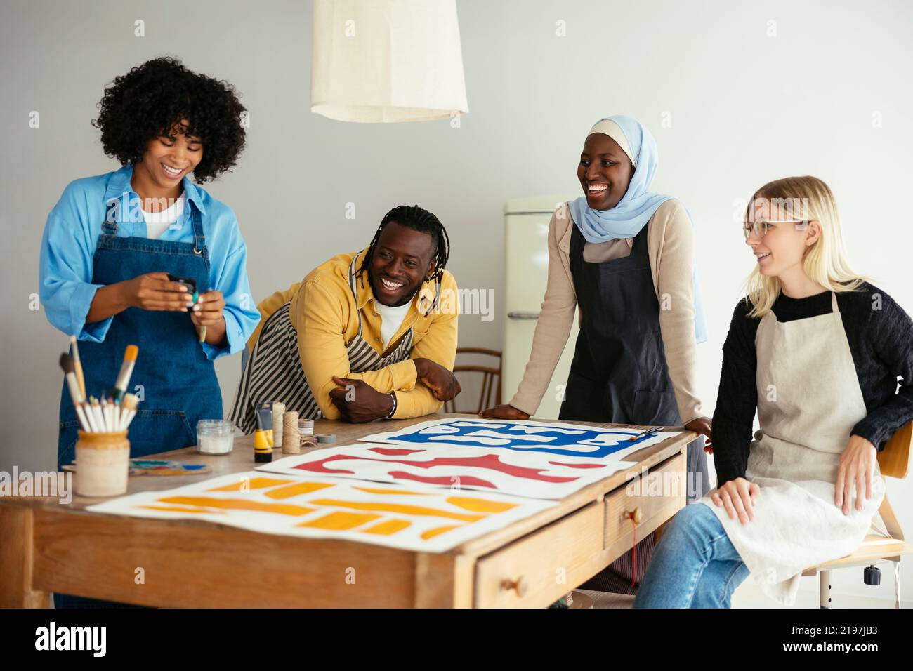 Artists laughing with paintings on desk in studio Stock Photo - Alamy