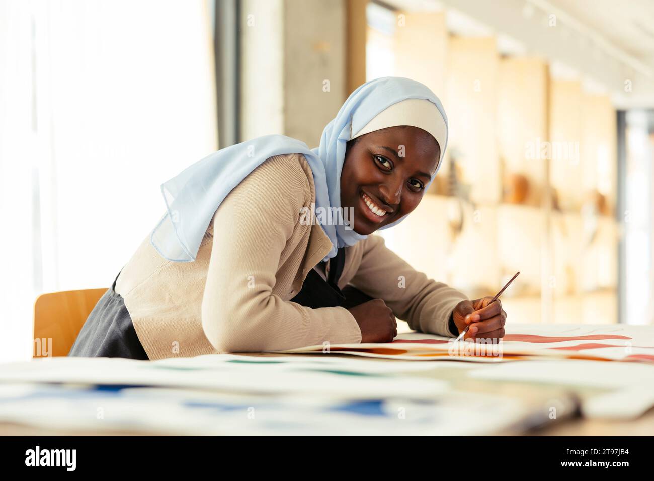 Smiling artist wearing headscarf painting with brush in studio Stock ...