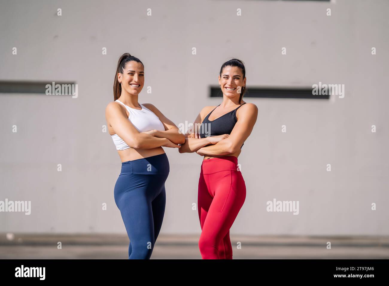 Active twin sisters with arms crossed standing together in front of ...