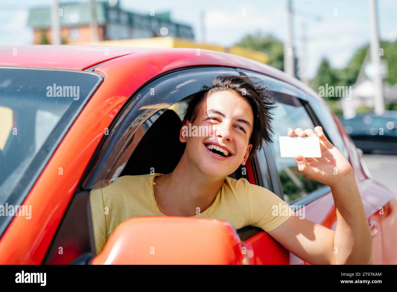 Smiling man showing driver's license and leaning out of car window ...