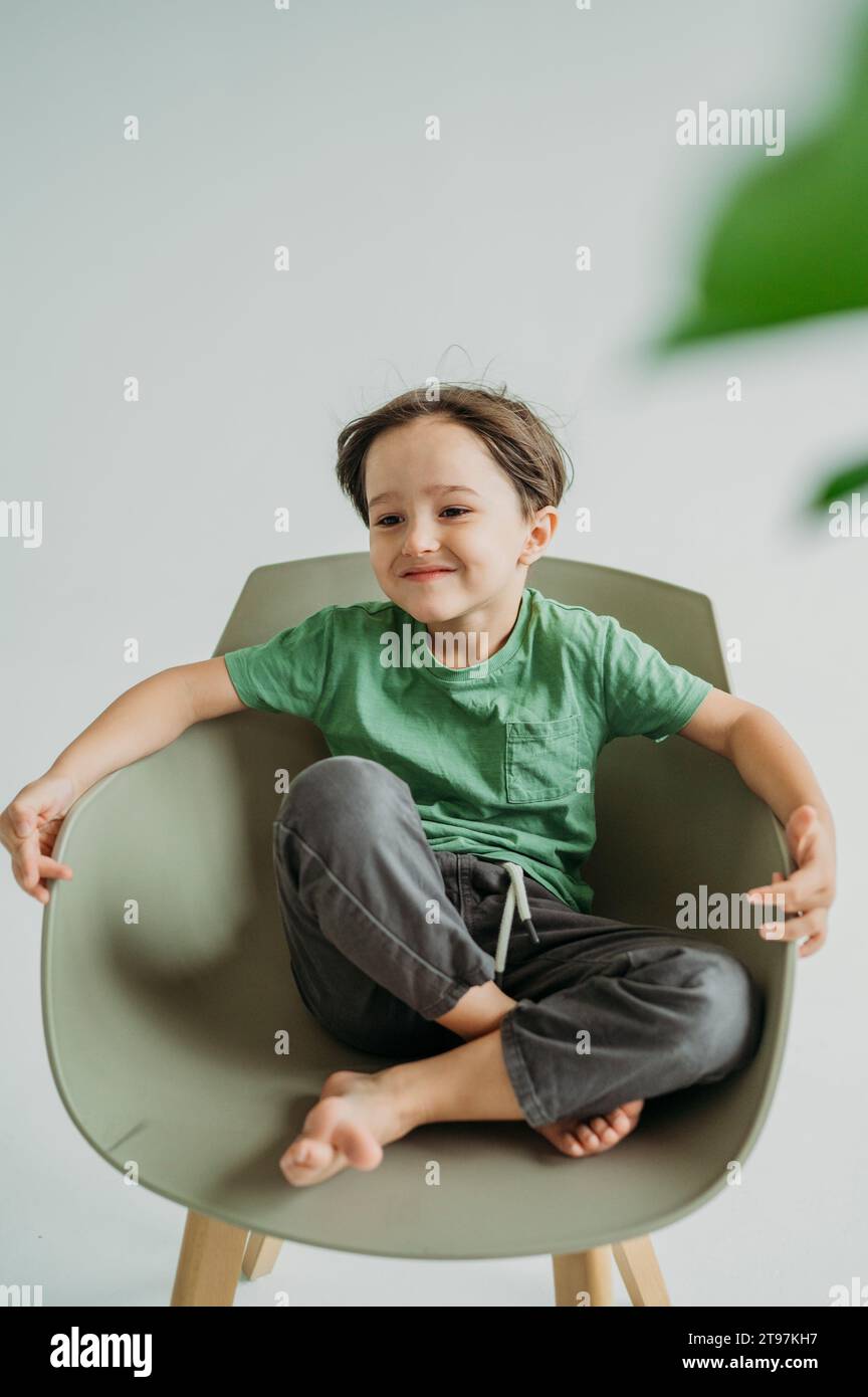 Happy boy sitting on chair in front of white wall Stock Photo - Alamy