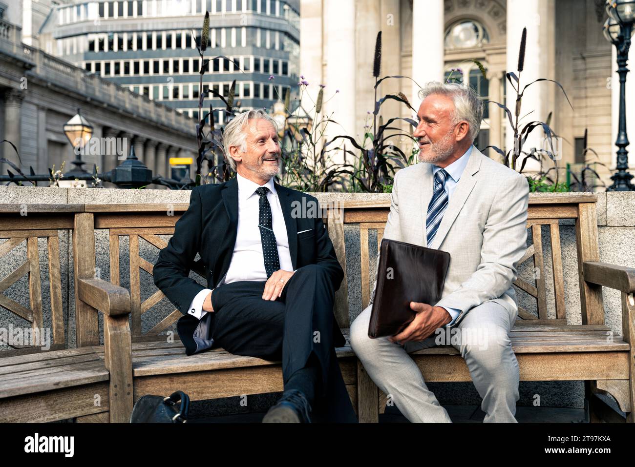 Happy senior businessmen having discussion together on bench in front ...