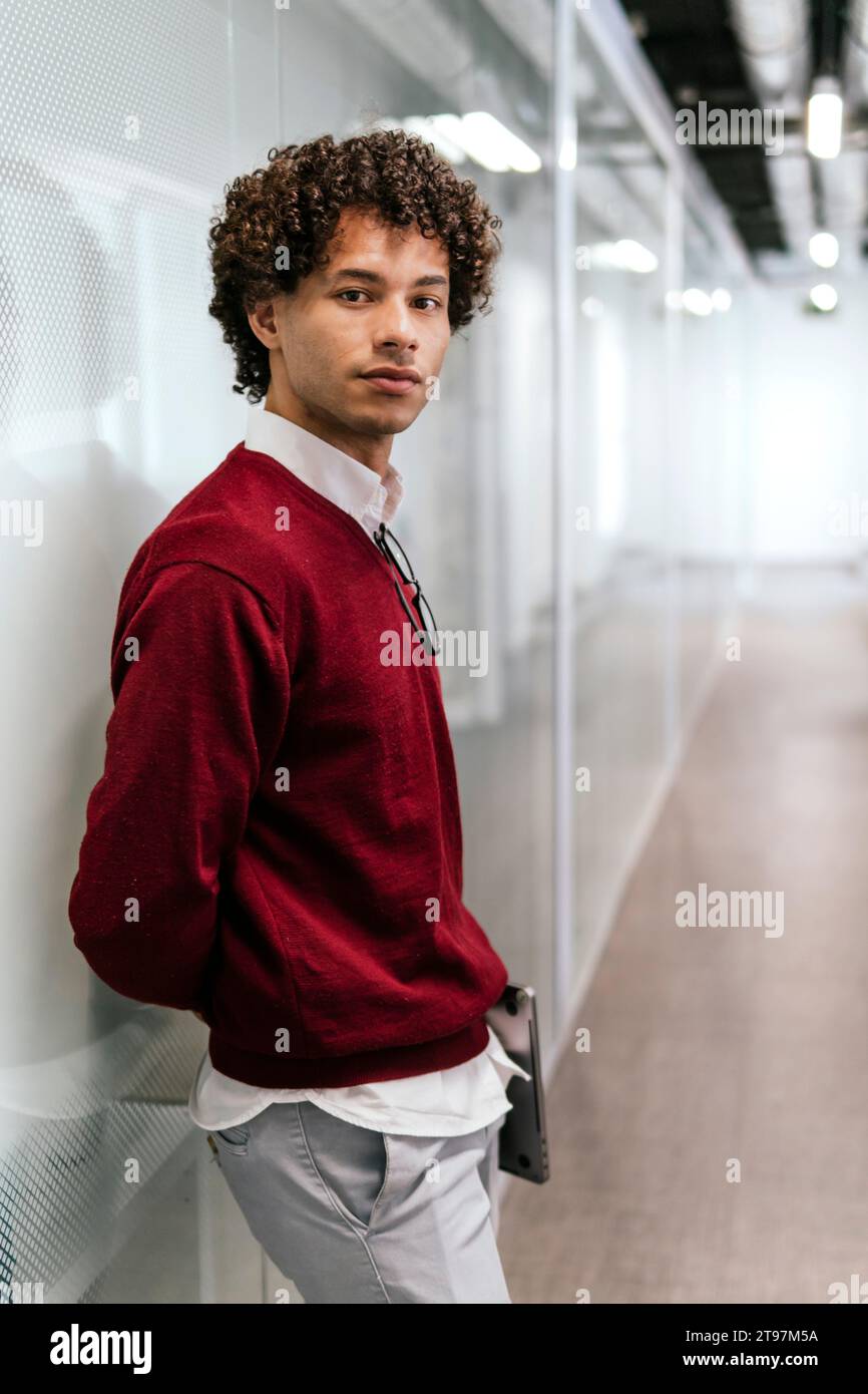 Businessman with hands behind back holding laptop and standing in front ...