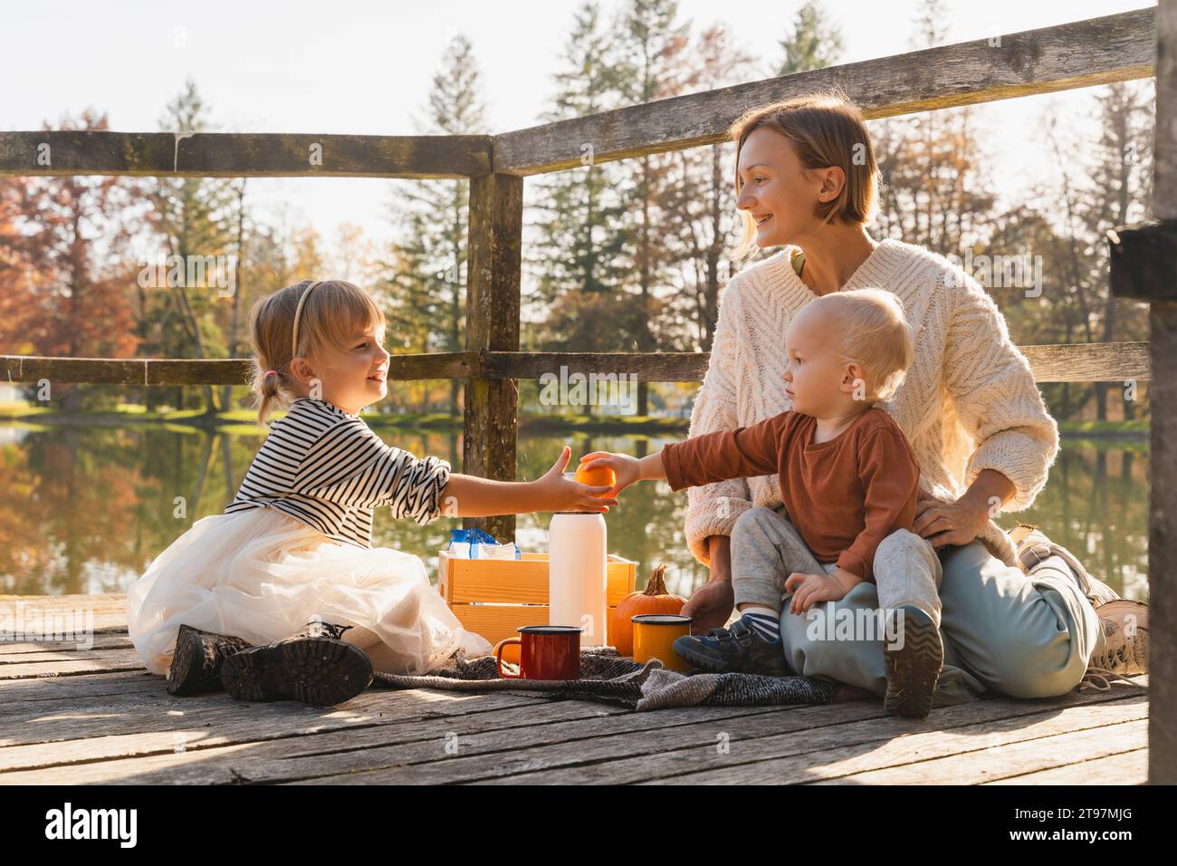 Mother with son giving tangerine to daughter on footbridge Stock Photo ...