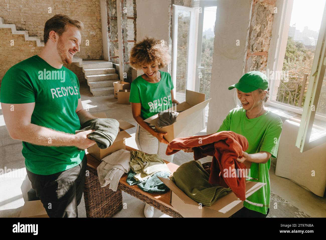 Happy activists examining and packing clothes in boxes at apartment ...