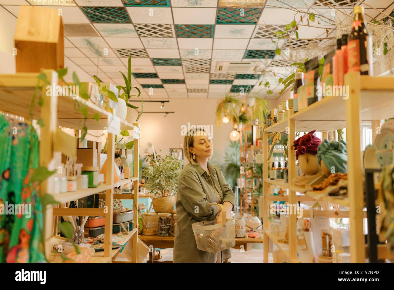 Blond woman with shopping basket looking around in store Stock Photo ...