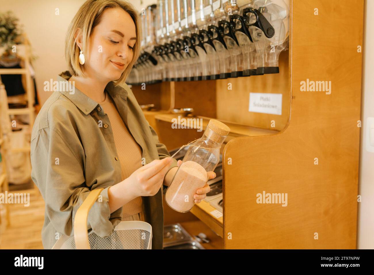 Smiling blond woman reading label on glass bottle in store Stock Photo ...