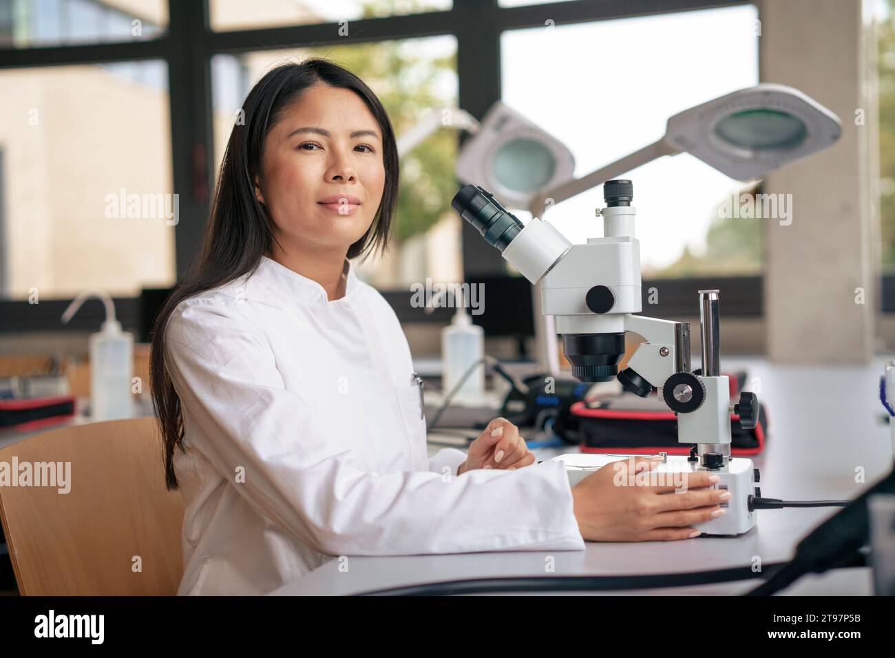 Smiling scientist sitting with microscope at desk Stock Photo - Alamy