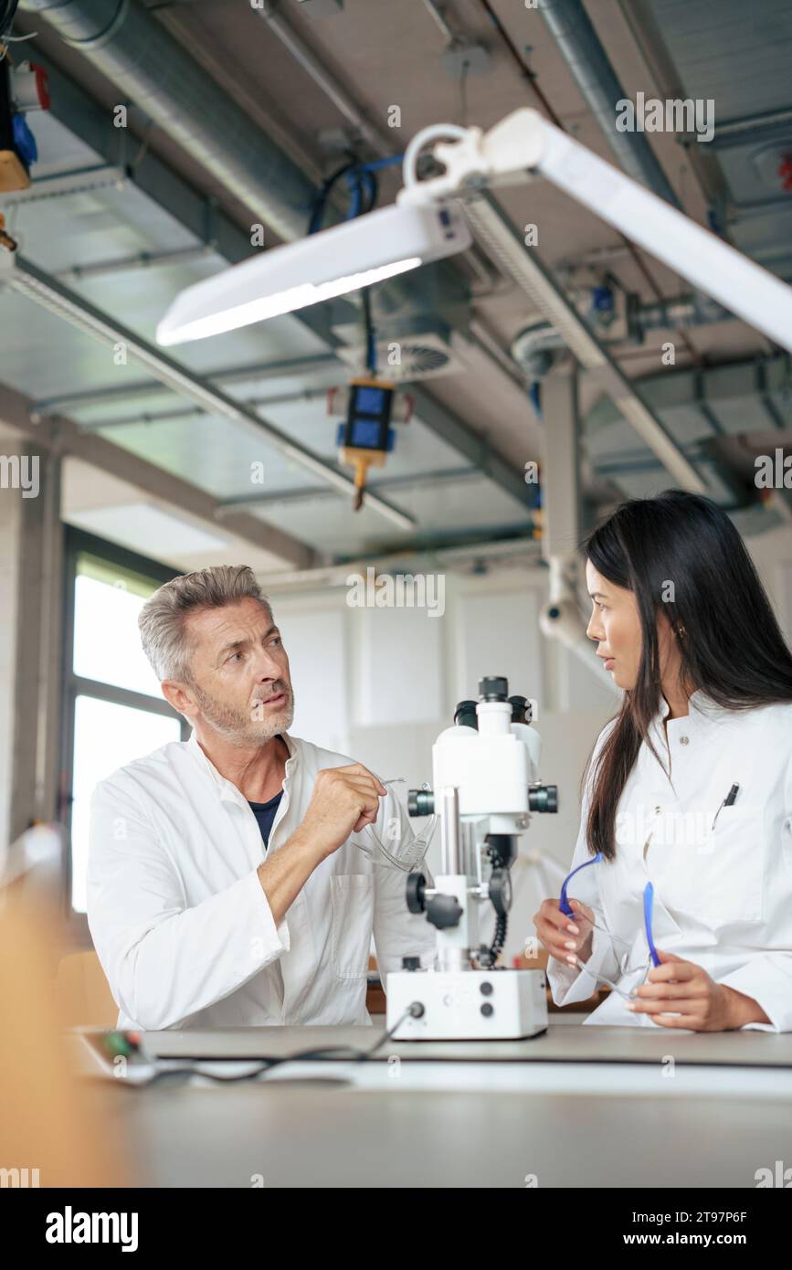 Scientists discussing with microscope at desk in laboratory Stock Photo ...