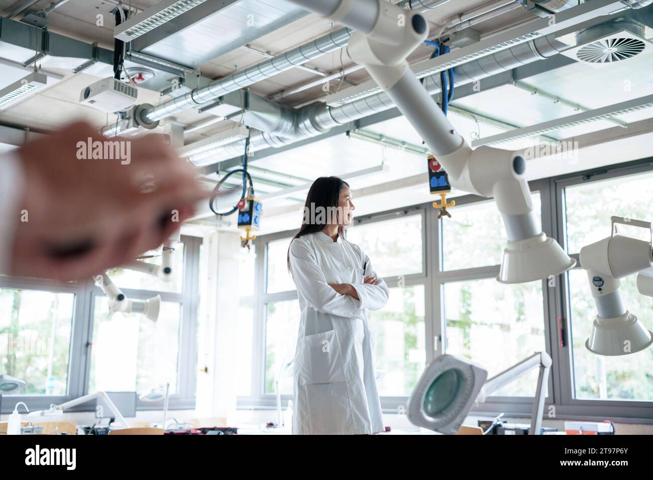 Thoughtful scientist standing near robotic arms in front of window at ...