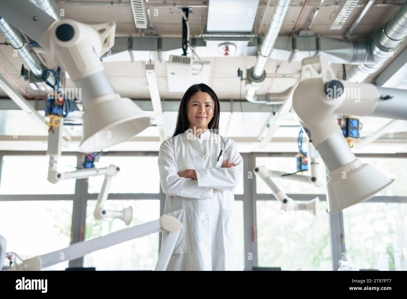 Smiling scientist standing amidst robotic arms Stock Photo - Alamy