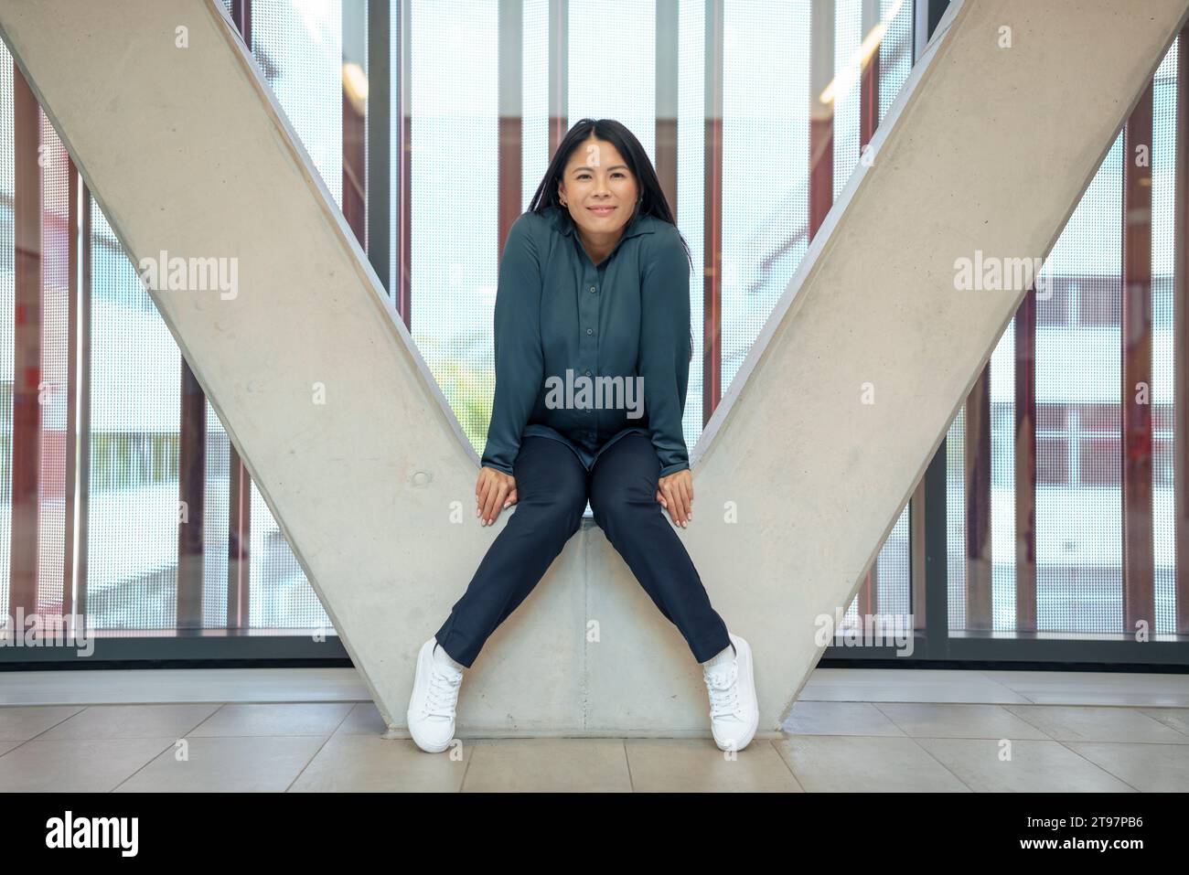Smiling businesswoman sitting on architectural column in office Stock ...