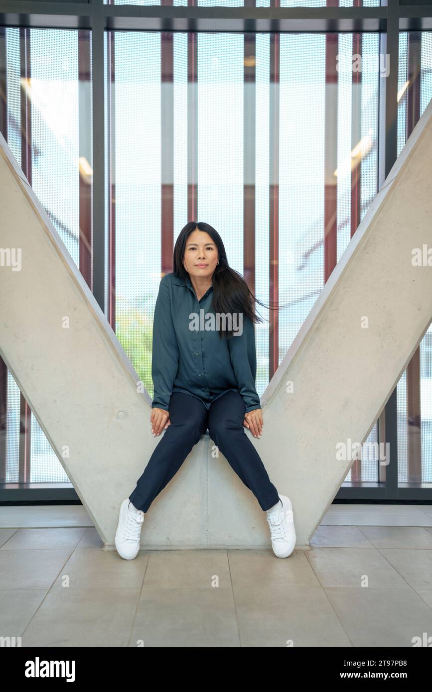 Businesswoman sitting on architectural column in office Stock Photo - Alamy