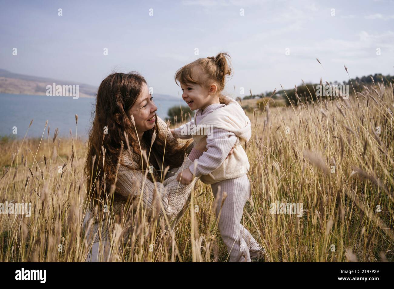 Smiling mother crouching and holding daughter in field Stock Photo - Alamy