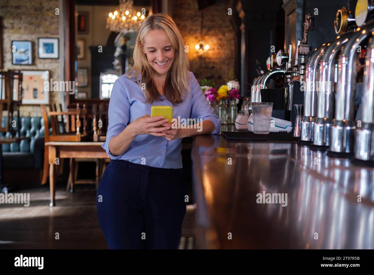 Smiling owner using smart phone near bar counter at pub Stock Photo - Alamy