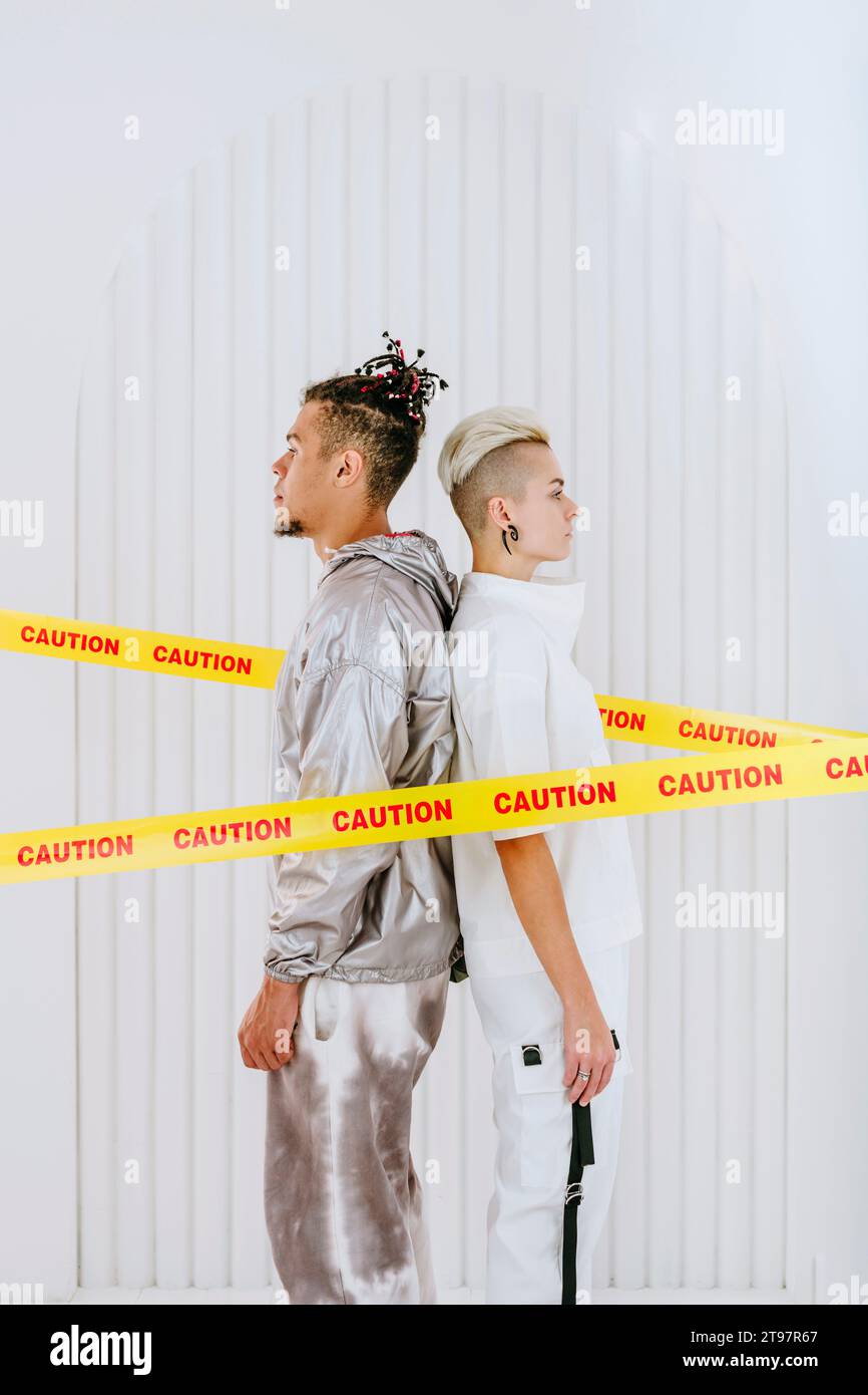 Young man and woman standing back to back between restriction tapes in ...