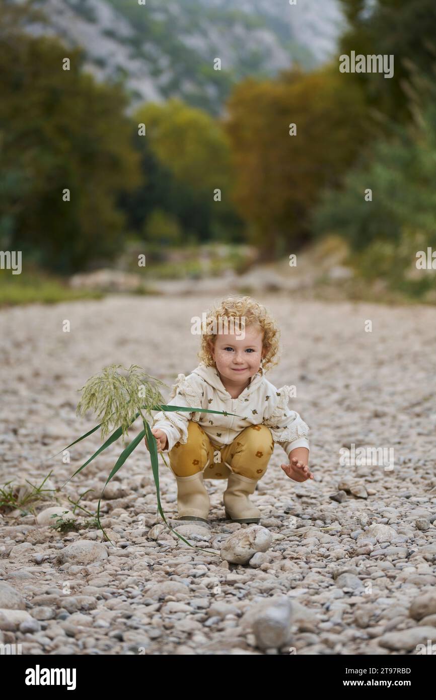 Smiling cute blond girl crouching with twig Stock Photo - Alamy