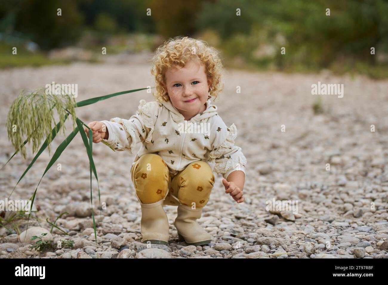 Smiling cute girl crouching with twig Stock Photo - Alamy
