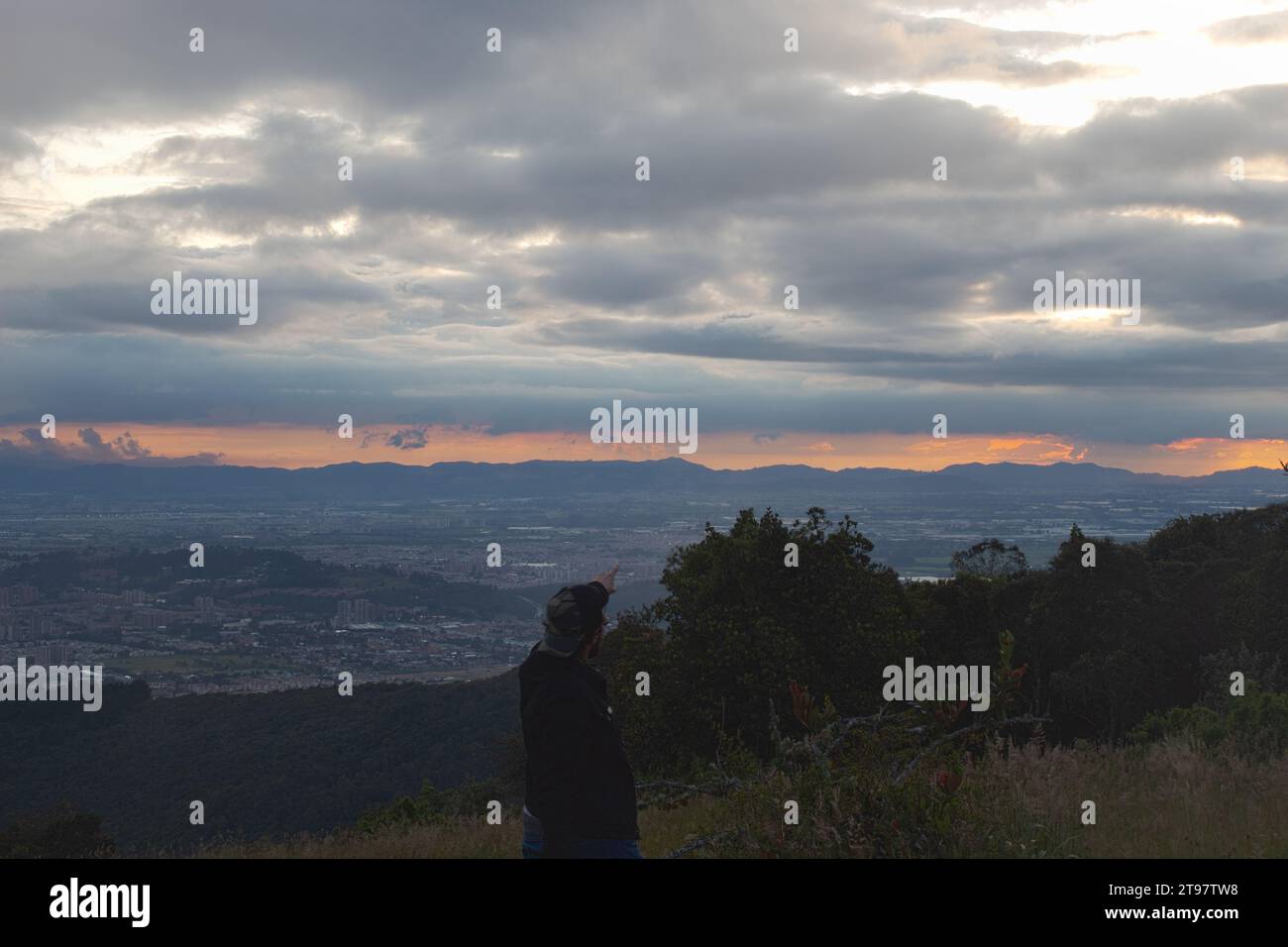 Young man pointing out to an orange sunset landscape with clouds and ...