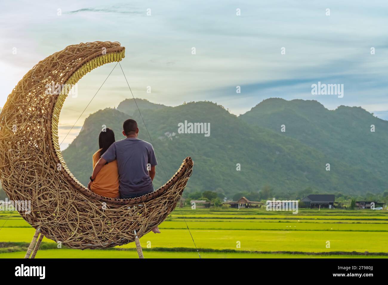 Happy couple sit on crescent moon chair made of rattan for relaxation ...