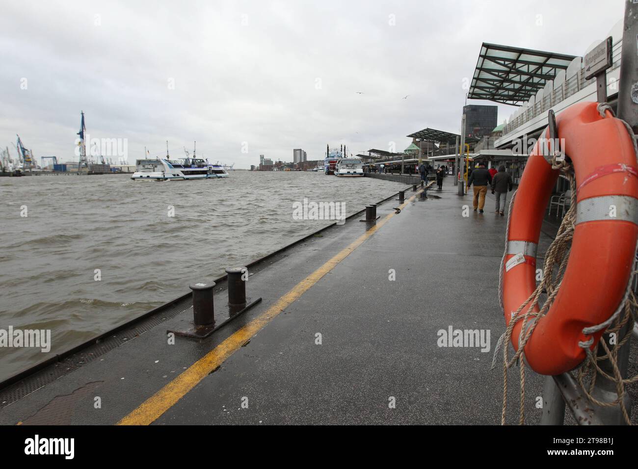 Passanten gehen bei Hamburger Schietwetter am Schiffsanleger Bei den Landungsbrücken entlang ...