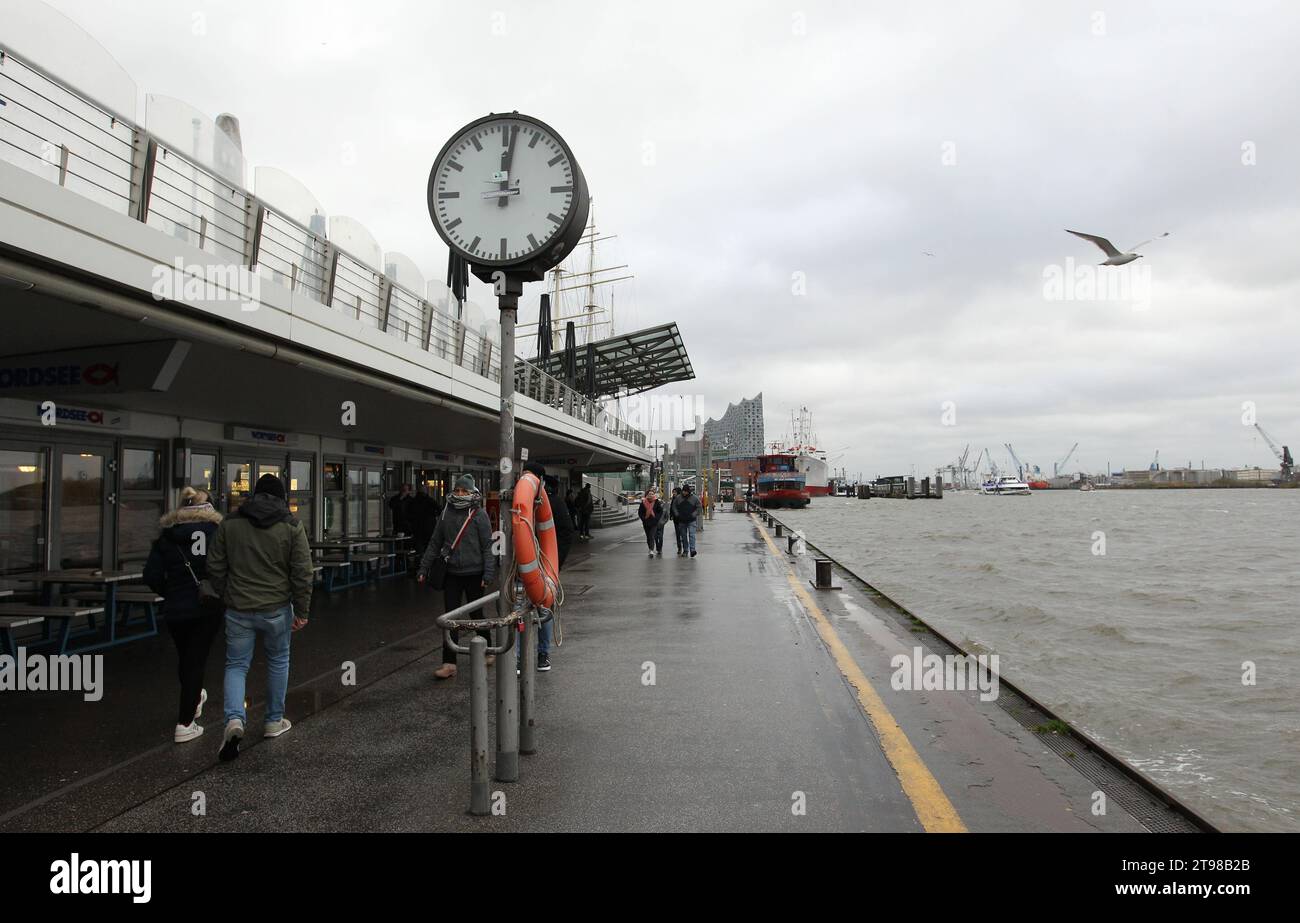Passanten gehen bei Hamburger Schietwetter am Schiffsanleger Bei den Landungsbrücken entlang. Im ...