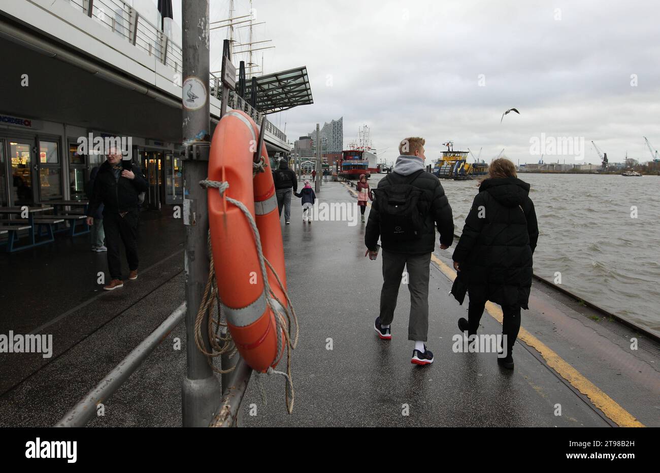 Passanten gehen bei Hamburger Schietwetter am Schiffsanleger Bei den Landungsbrücken entlang ...