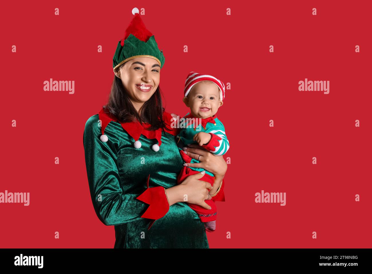 Young mother and cute little baby dressed as elves on red background ...