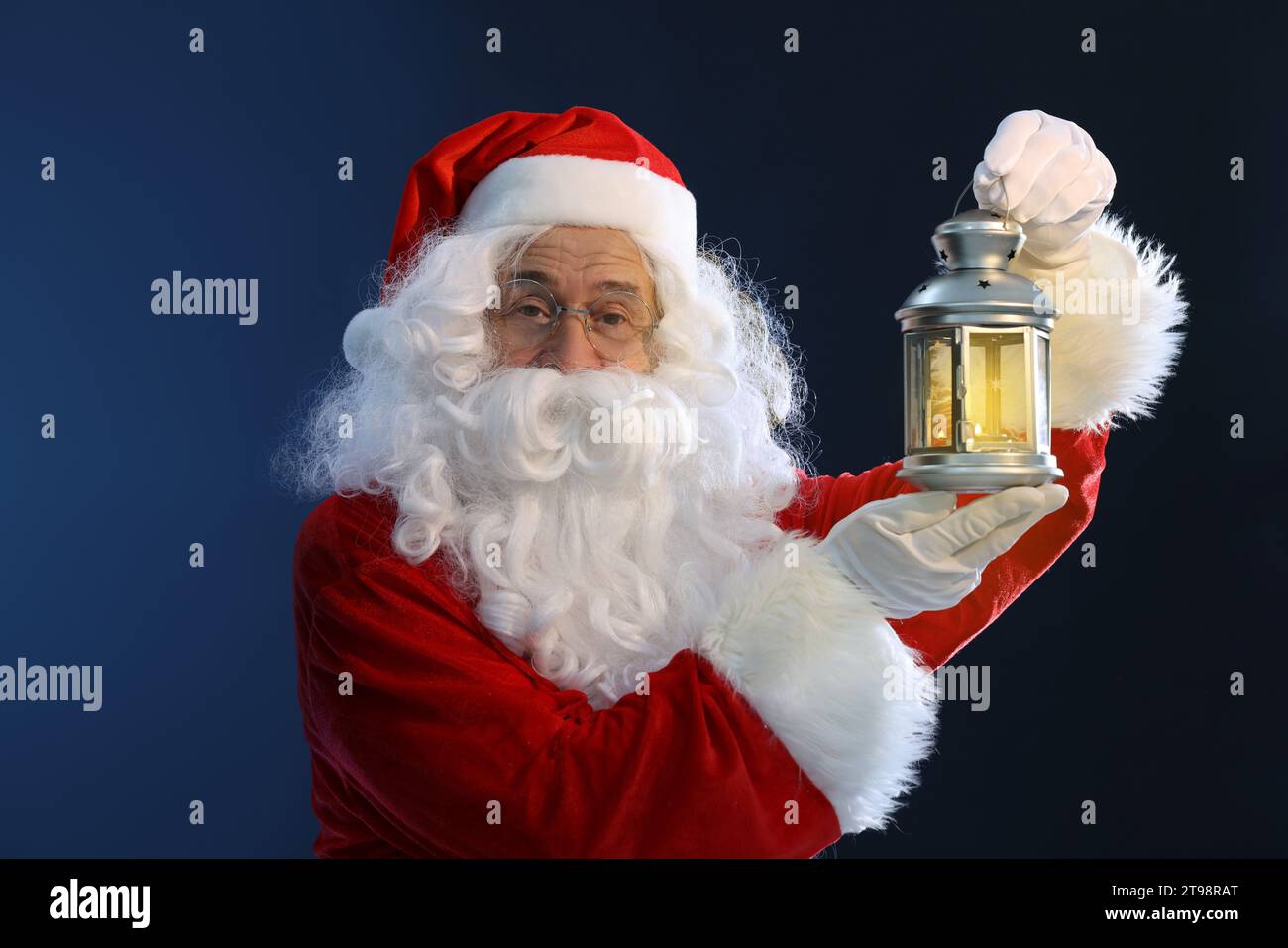 Santa Claus holding Christmas lantern with burning candle on dark blue ...
