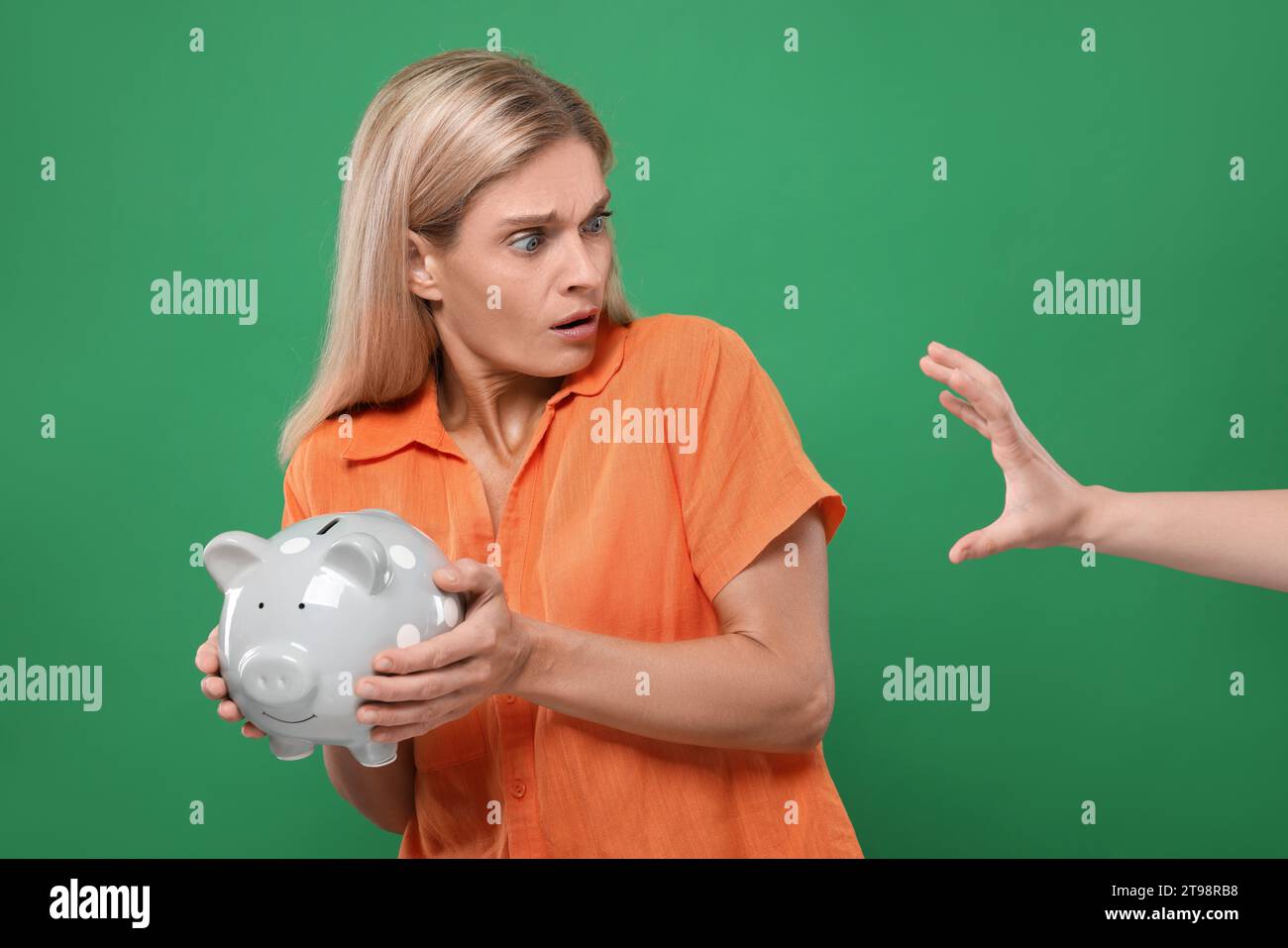 Scammer taking piggy bank from scared woman on green background. Be ...