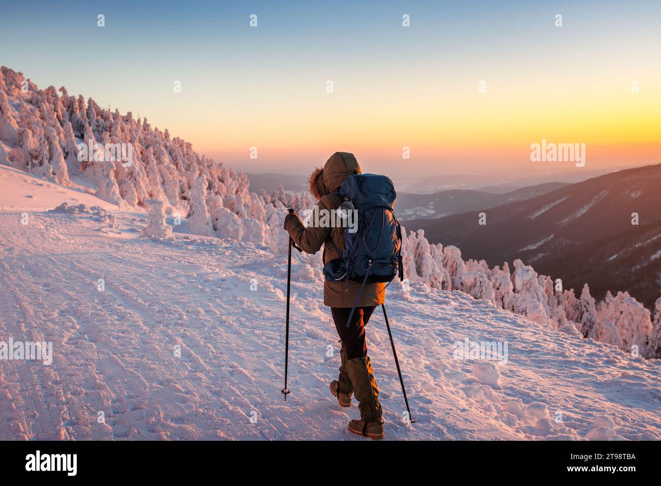 Hiking in snow at winter mountain during sunset. Woman with backpack ...