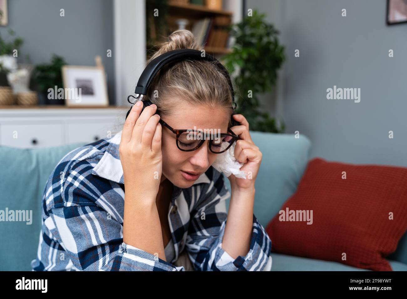 Young sad girl sitting alone at home on sofa listening to sad music on ...