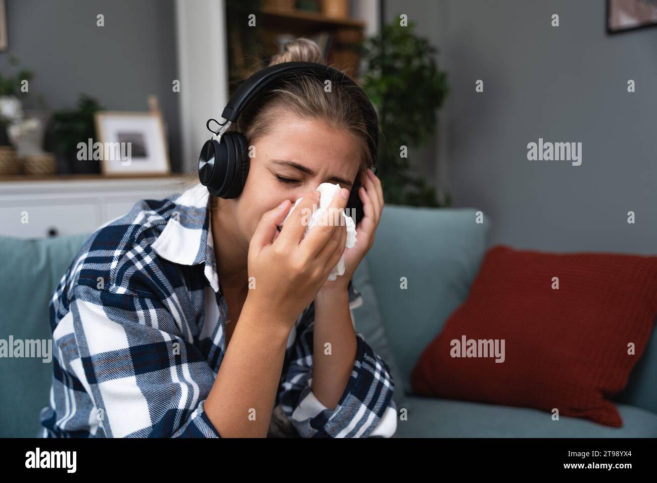 Young sad girl sitting alone at home on sofa listening to sad music on ...