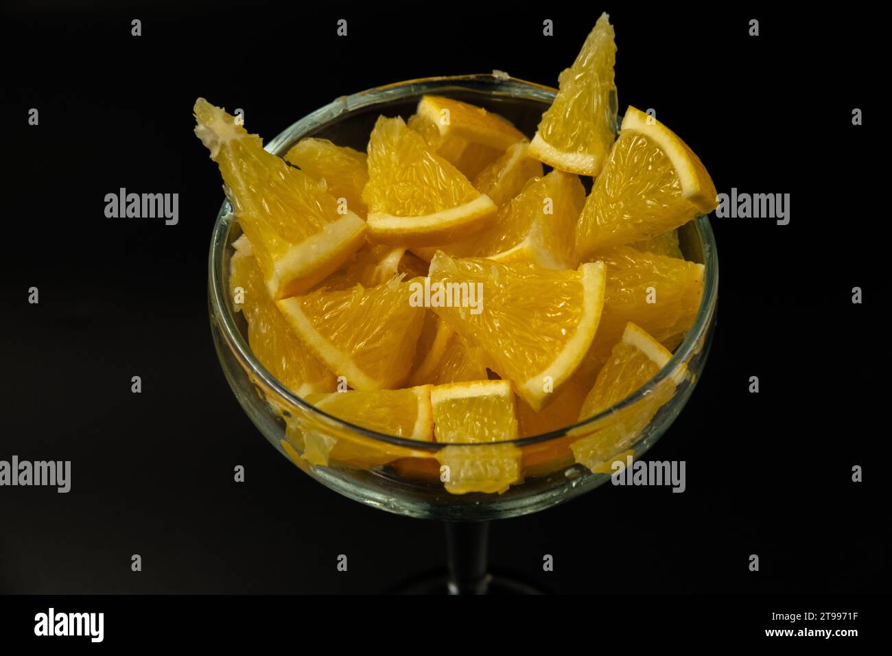 Orange pieces sliced into small triangles in a glass bowl on a black ...