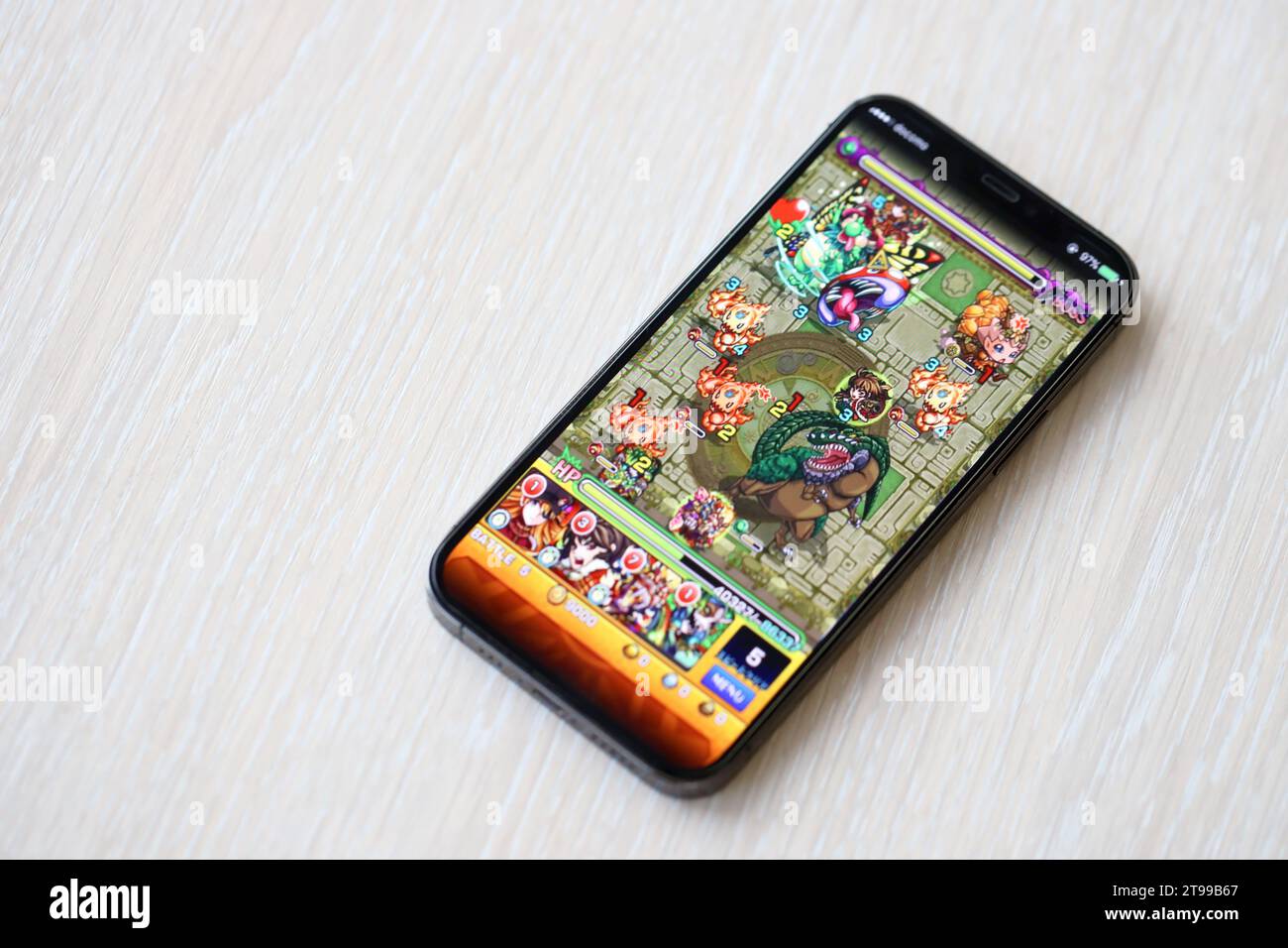 Monster Strike mobile iOS game on iPhone 15 smartphone screen on wooden ...