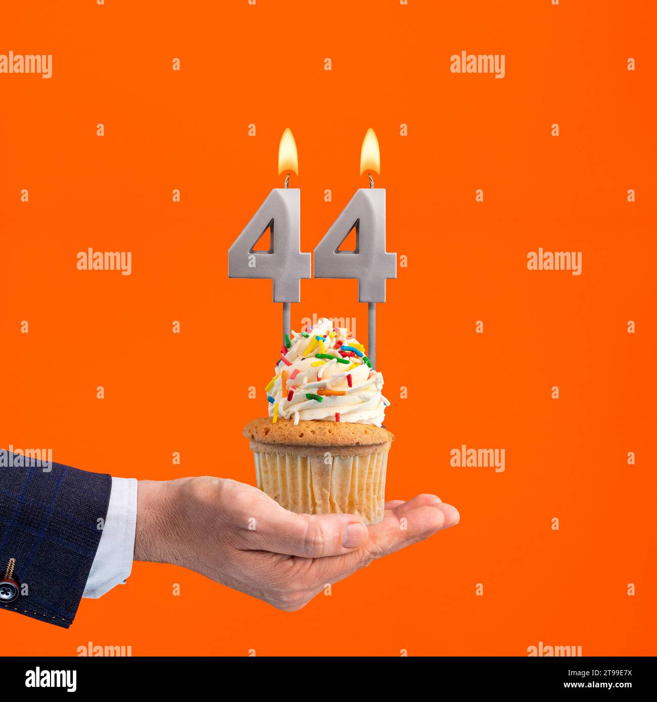Hand holding birthday cupcake with number 44 candle - background orange ...